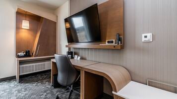 Quarto de hotel moderno com escrivaninha curva, TV de tela plana na parede, cantinho para café e termostato na parede.