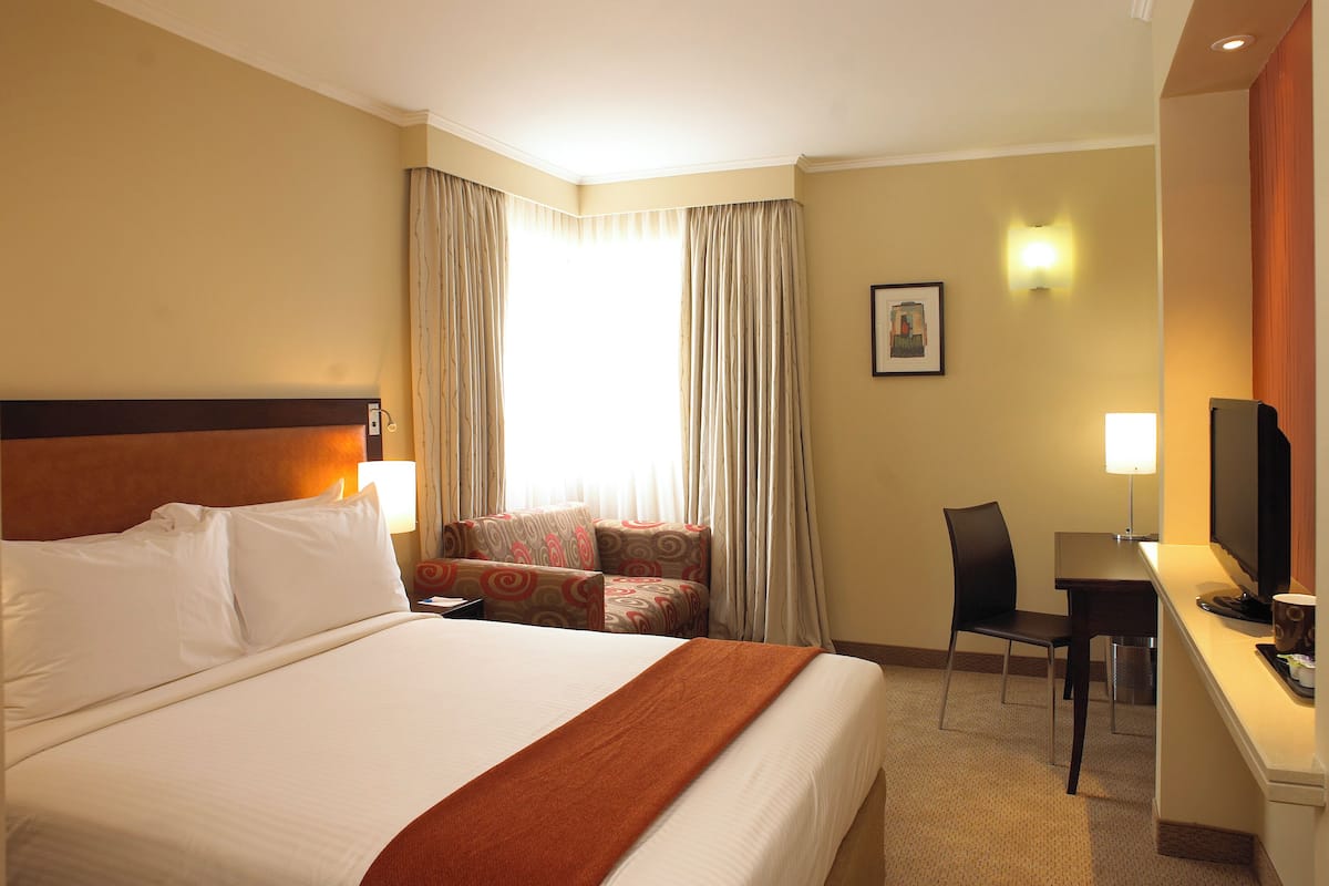 Quarto de hotel com uma cama grande, uma escrivaninha com cadeira, televisão e um quadro na parede.