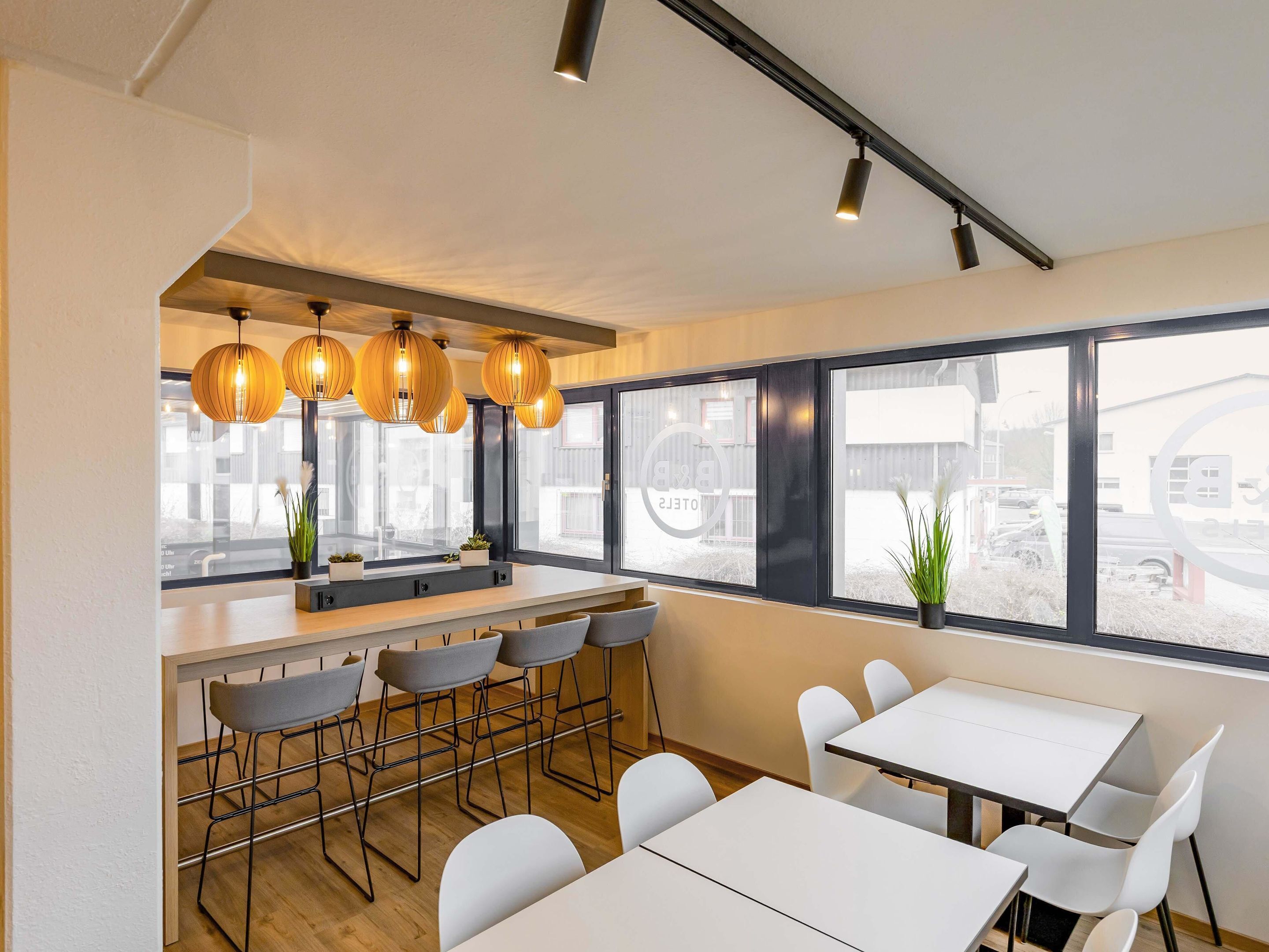 Decoração moderna com área de bar, mesas brancas e uma grande janela com vista.
