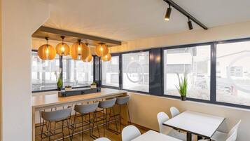 Decoração moderna com área de bar, mesas brancas e uma grande janela com vista.