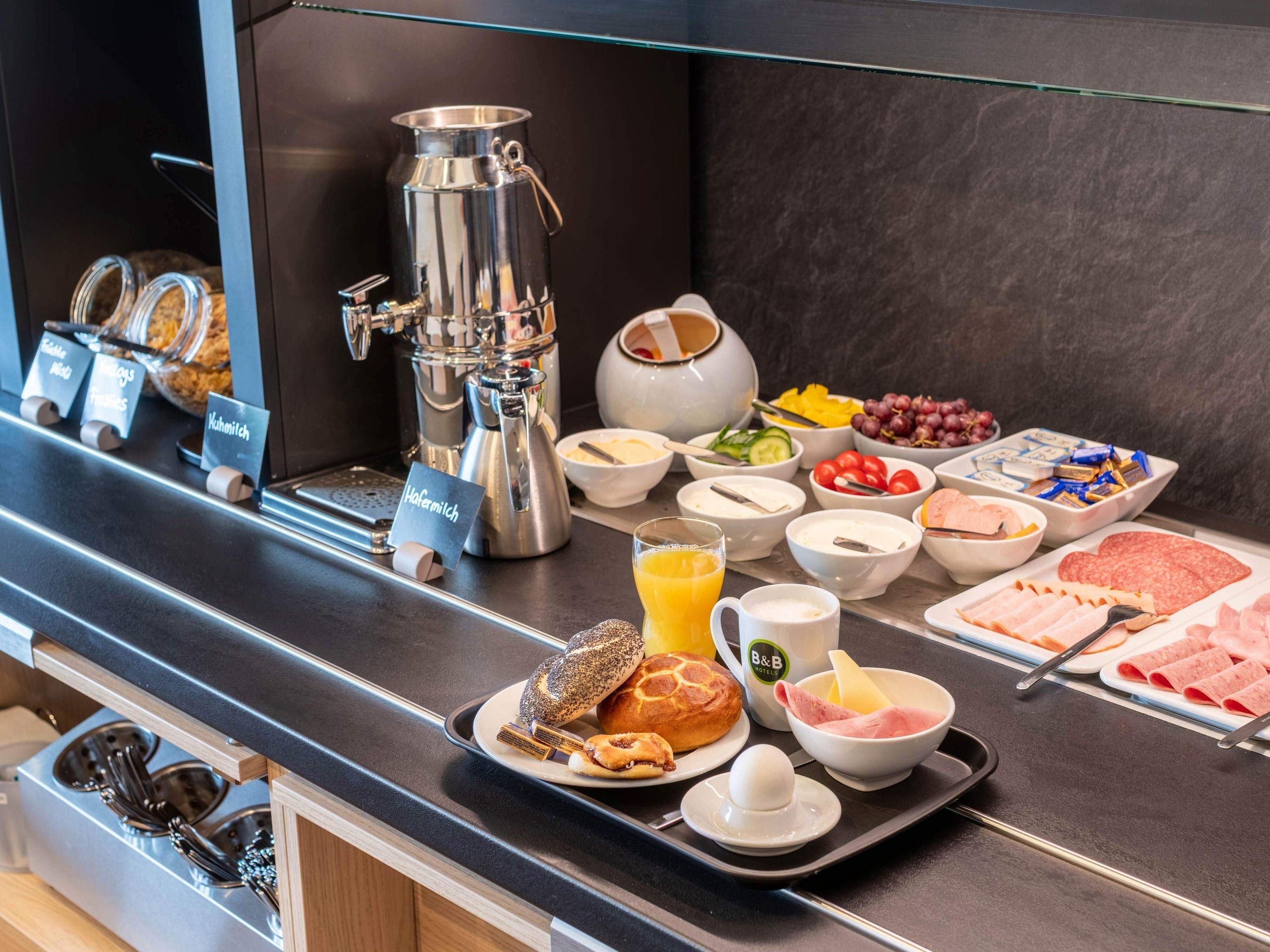 Buffet com diversos alimentos, incluindo pão, queijo, carnes e frutas.