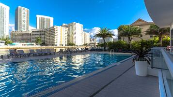 Piscina com espreguiçadeiras, um horizonte urbano ao fundo e palmeiras.
