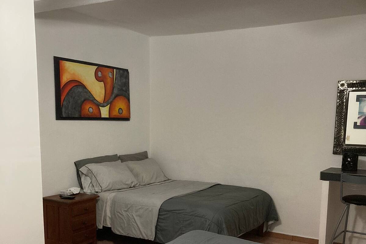 Quarto com duas camas, mesa de cabeceira, escrivaninha e ventoinha no teto.