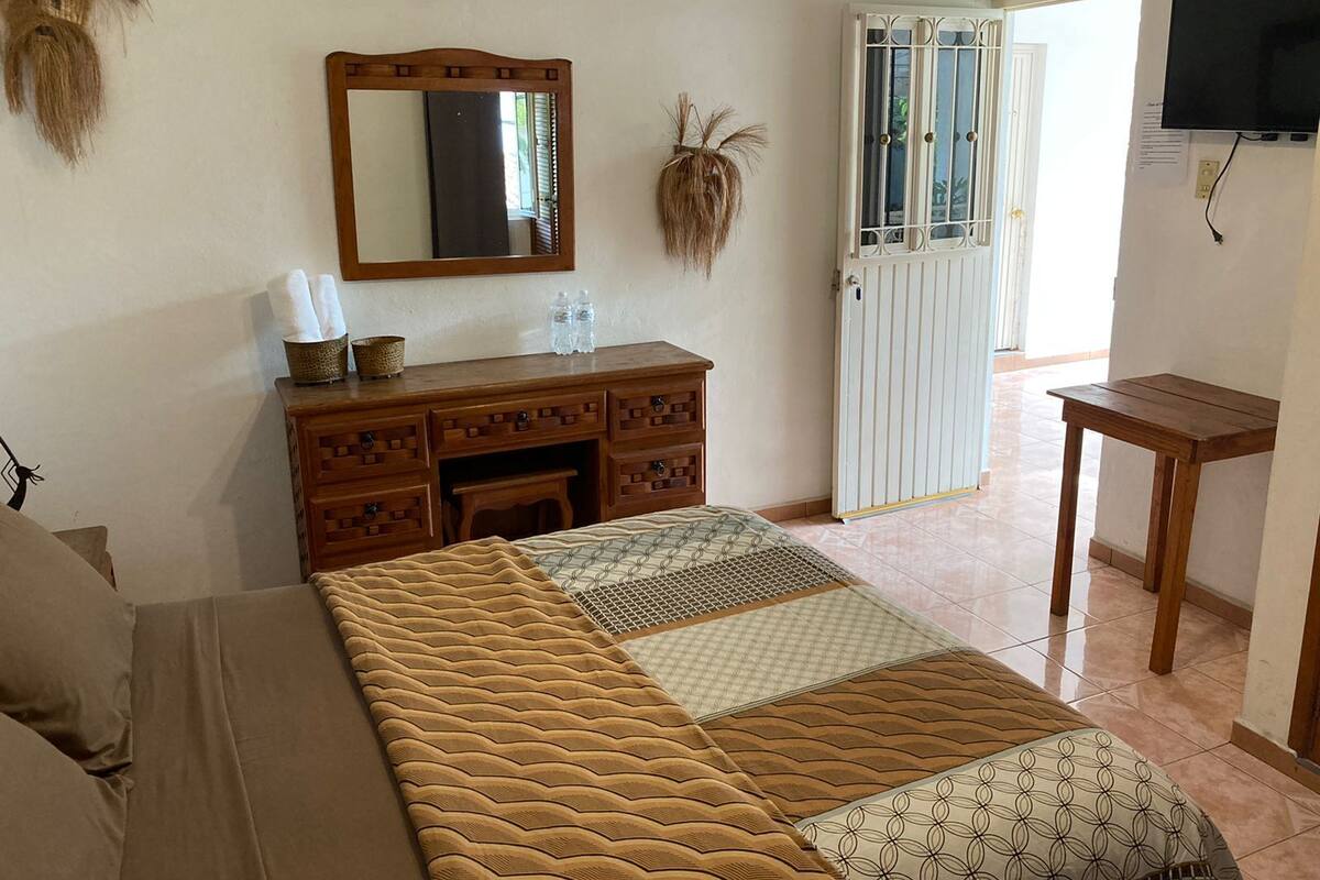 Quarto com cama, penteadeira, espelho e televisão na parede.