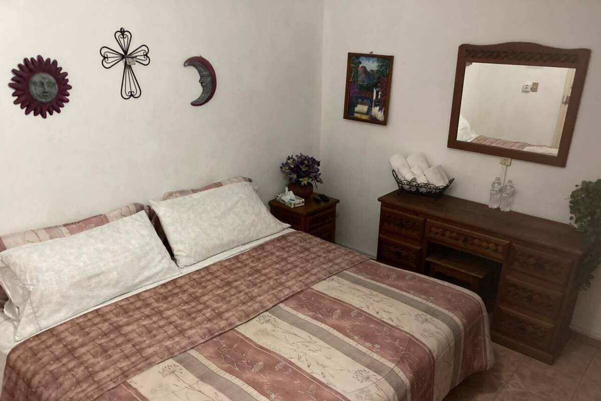 Quarto com cama, mesa de cabeceira, cômoda, espelho e decorações nas paredes.