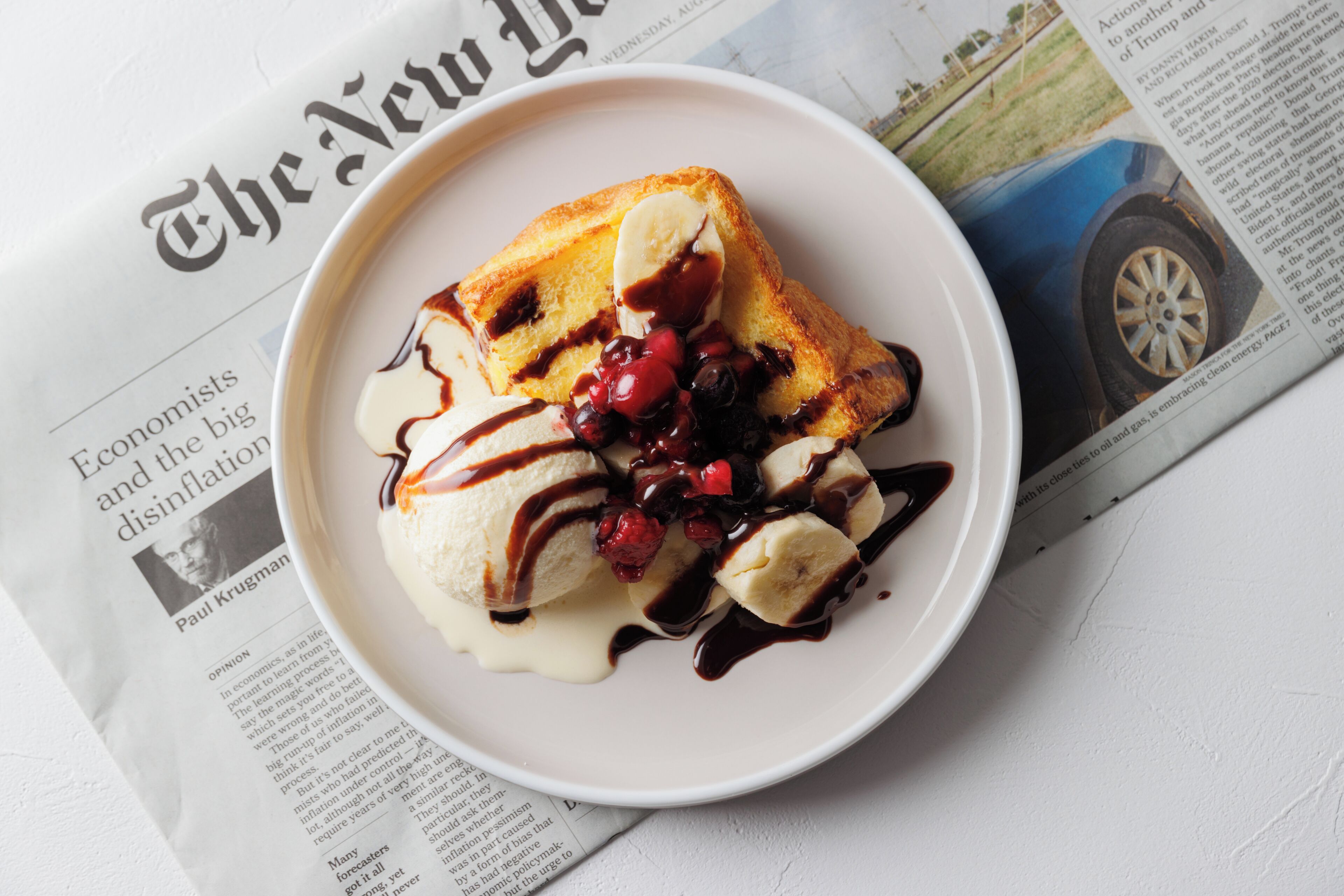 Prato de sobremesa com sorvete e frutas vermelhas sobre um jornal.