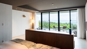 Quarto moderno com uma grande janela, uma cama, mesa de cabeceira e vista para o oceano.