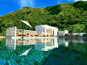 Uma área de piscina com água cristalina, espreguiçadeiras e um edifício de fachada branca.