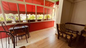Quarto com parede vermelha, janela com persianas, piso de madeira e duas cadeiras.