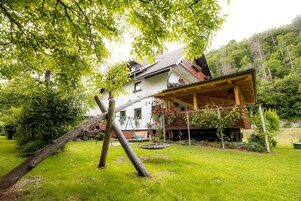 Uma casa com telhado inclinado, cercada por vegetação exuberante e uma árvore caída.