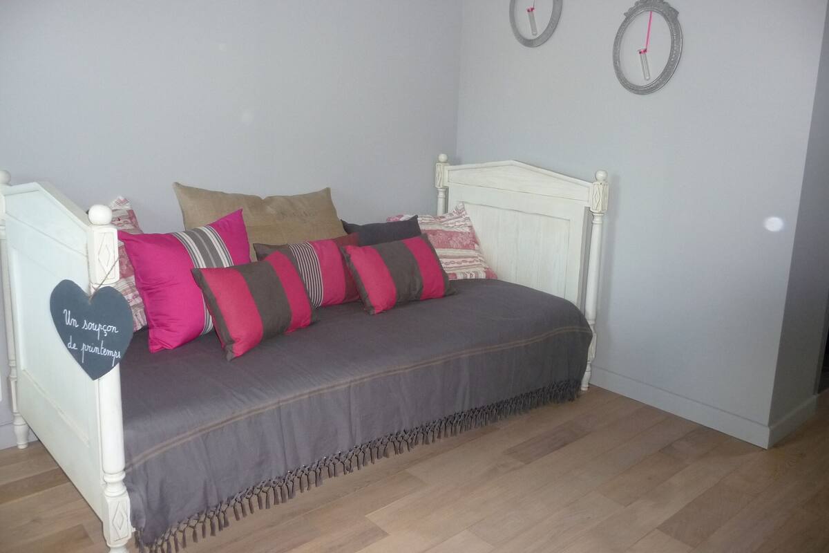 Cama com cabeceira, várias almofadas, edredom escuro e uma decoração em formato de coração ao lado.