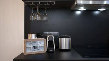 Uma bancada de cozinha com cafeteira, torradeira e chaleira. Há copos de vinho pendurados acima da bancada e um letreiro emoldurado sobre ela.