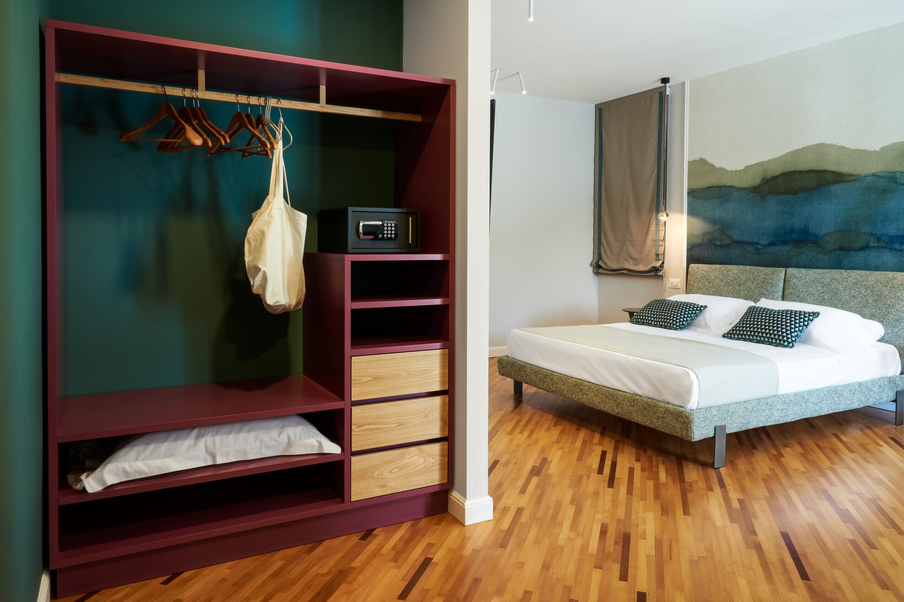 Quarto com cama, guarda-roupa cheio de roupas penduradas, micro-ondas e um quadro na parede.