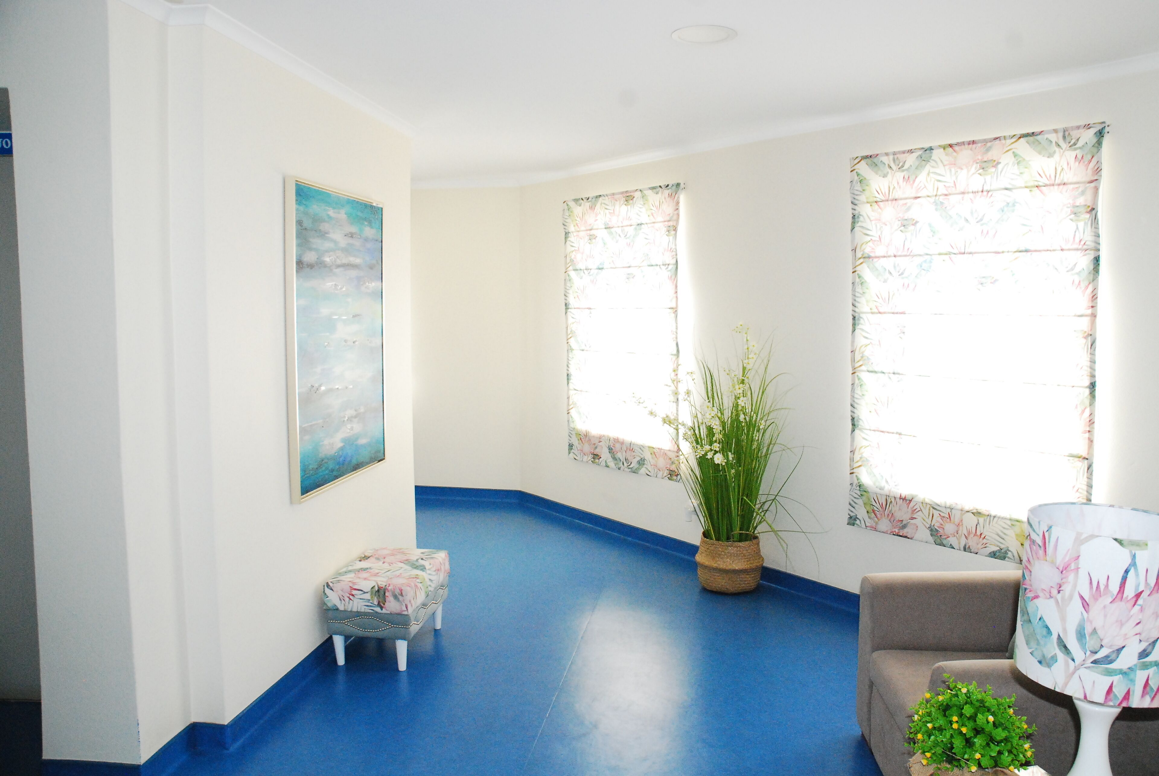 Um corredor com piso azul, um banco, uma planta em vaso e um sofá.