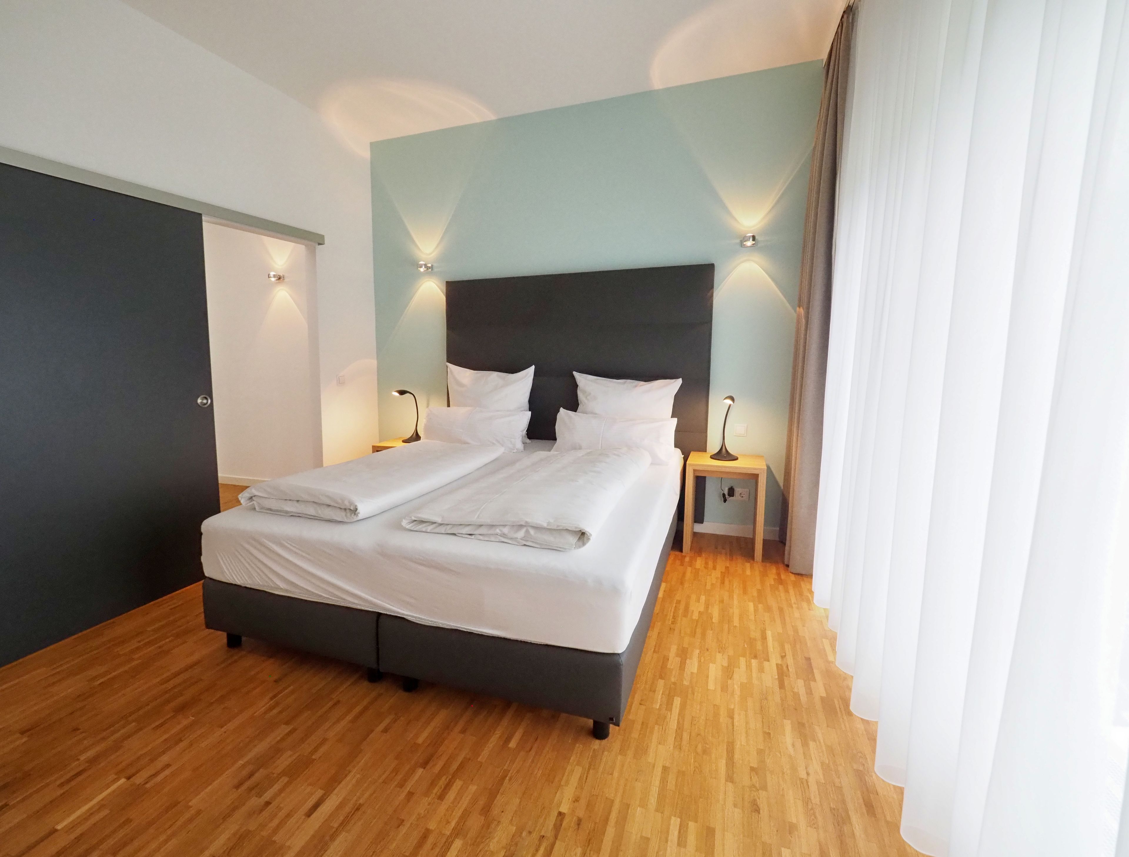 Quarto de hotel moderno com uma cama grande, duas mesas de cabeceira e uma mesinha de apoio.