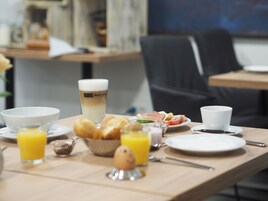 Uma mesa de café da manhã com uma xícara de café, croissants, um prato de presunto e queijo e um copo de suco de laranja.