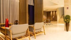 Um saguão moderno de hotel com balcão de recepção, área de estar e uma escadaria.