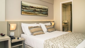 Quarto de hotel com cama, mesa de cabeceira, luminária e um quadro na parede.
