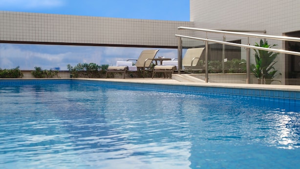 Piscina com espreguiçadeiras e guarda-corpo de vidro.