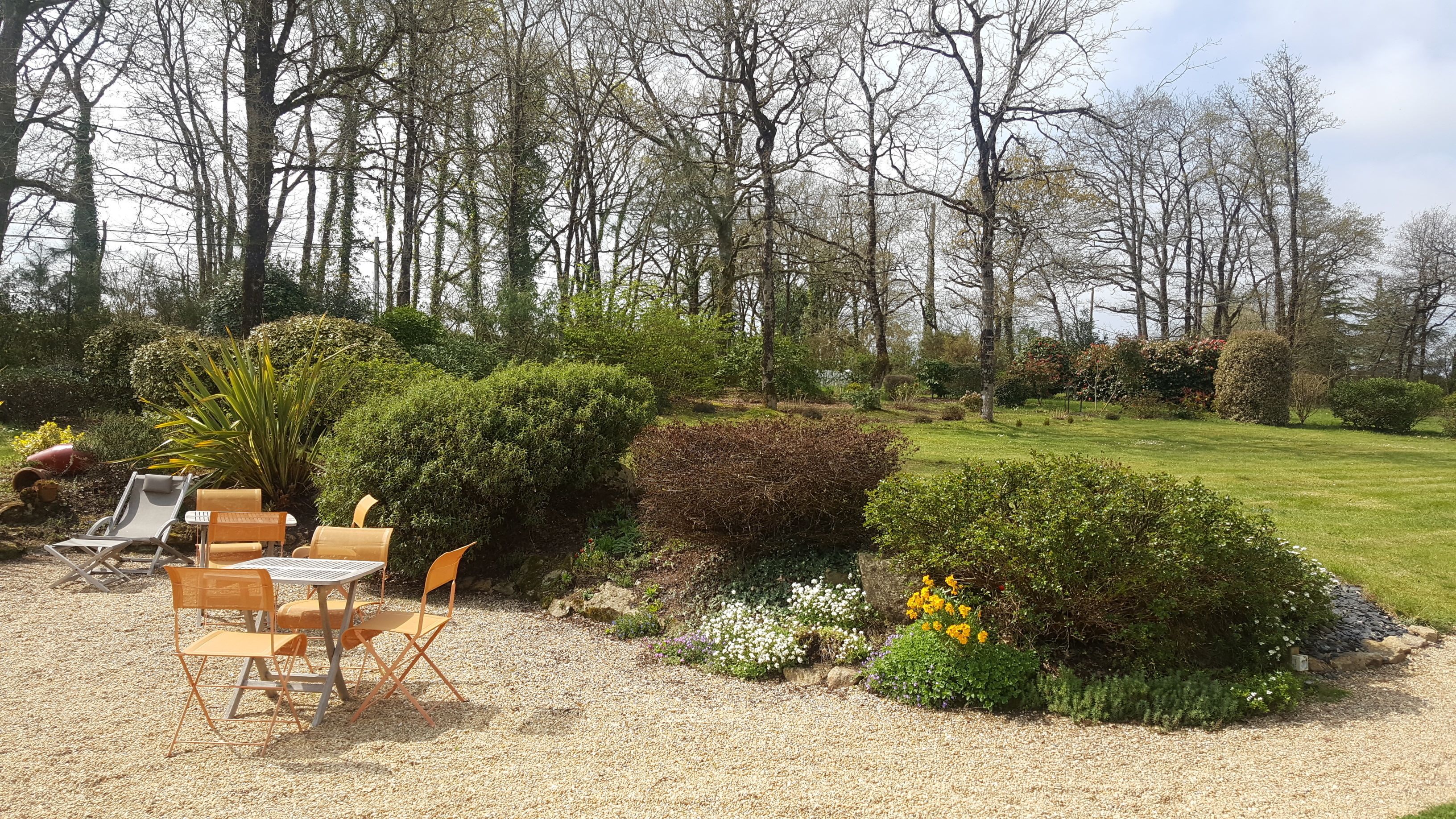 Um jardim com mesa e cadeiras, cercado por diversas plantas e árvores.