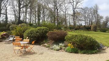 Um jardim com mesa e cadeiras, cercado por diversas plantas e árvores.