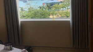 Quarto com uma grande janela que oferece vista para uma área costeira, com colinas e barcos.