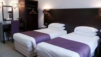 Quarto de hotel com duas camas, uma escrivaninha, uma cadeira e um espelho.