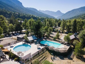Um resort com duas piscinas, cercado por árvores e montanhas.