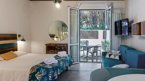 Quarto de hotel com cama, sofá, televisão e varanda com vista para árvores.