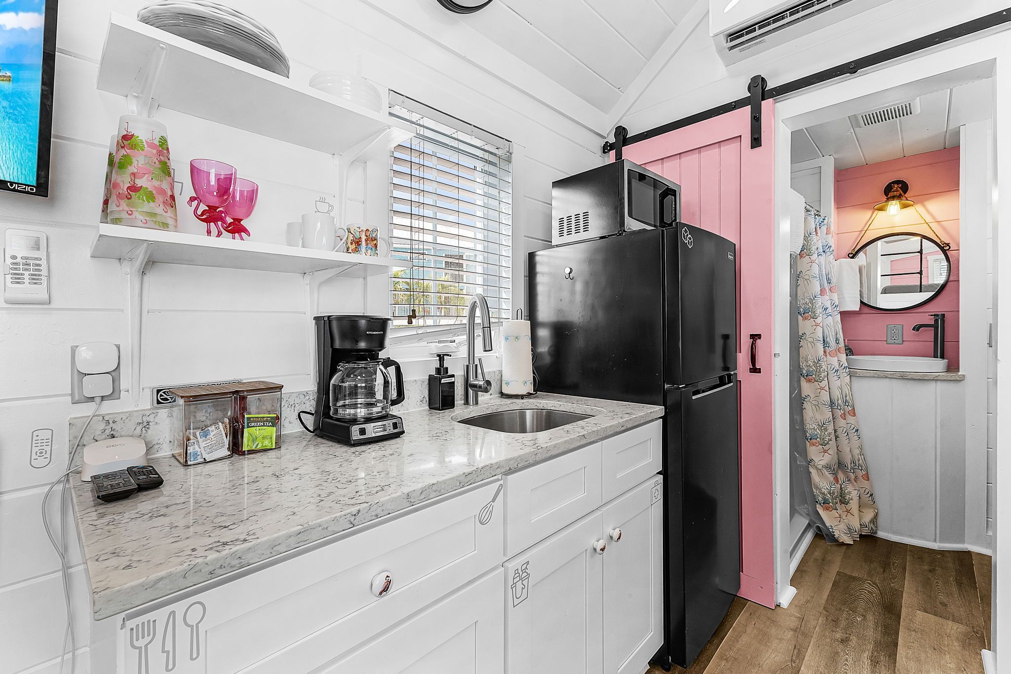 Uma cozinha moderna com armários brancos, uma geladeira preta e uma parede com detalhes em rosa.