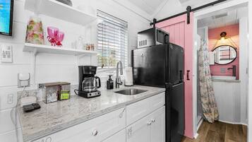 Uma cozinha moderna com armários brancos, uma geladeira preta e uma parede com detalhes em rosa.