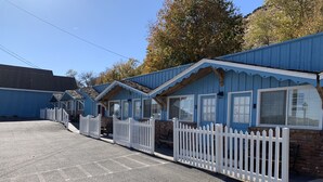 Uma fileira de cabanas azuis com cercas brancas, cada uma com base de tijolos e telhado inclinado.