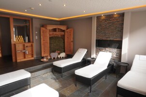 Um espaço de spa com duas poltronas confortáveis, um armário de madeira com velas e uma parede de pedra.