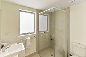 Uma casa de banho moderna com cabine de duche em vidro, lavatório branco e sanita.