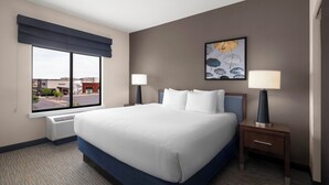 Quarto de hotel com uma cama grande, duas mesas de cabeceira com luminárias, uma janela com vista para a cidade e um quadro na parede.