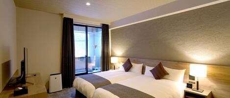 Quarto de hotel com duas camas, uma escrivaninha com computador, uma luminária e vista para o exterior.