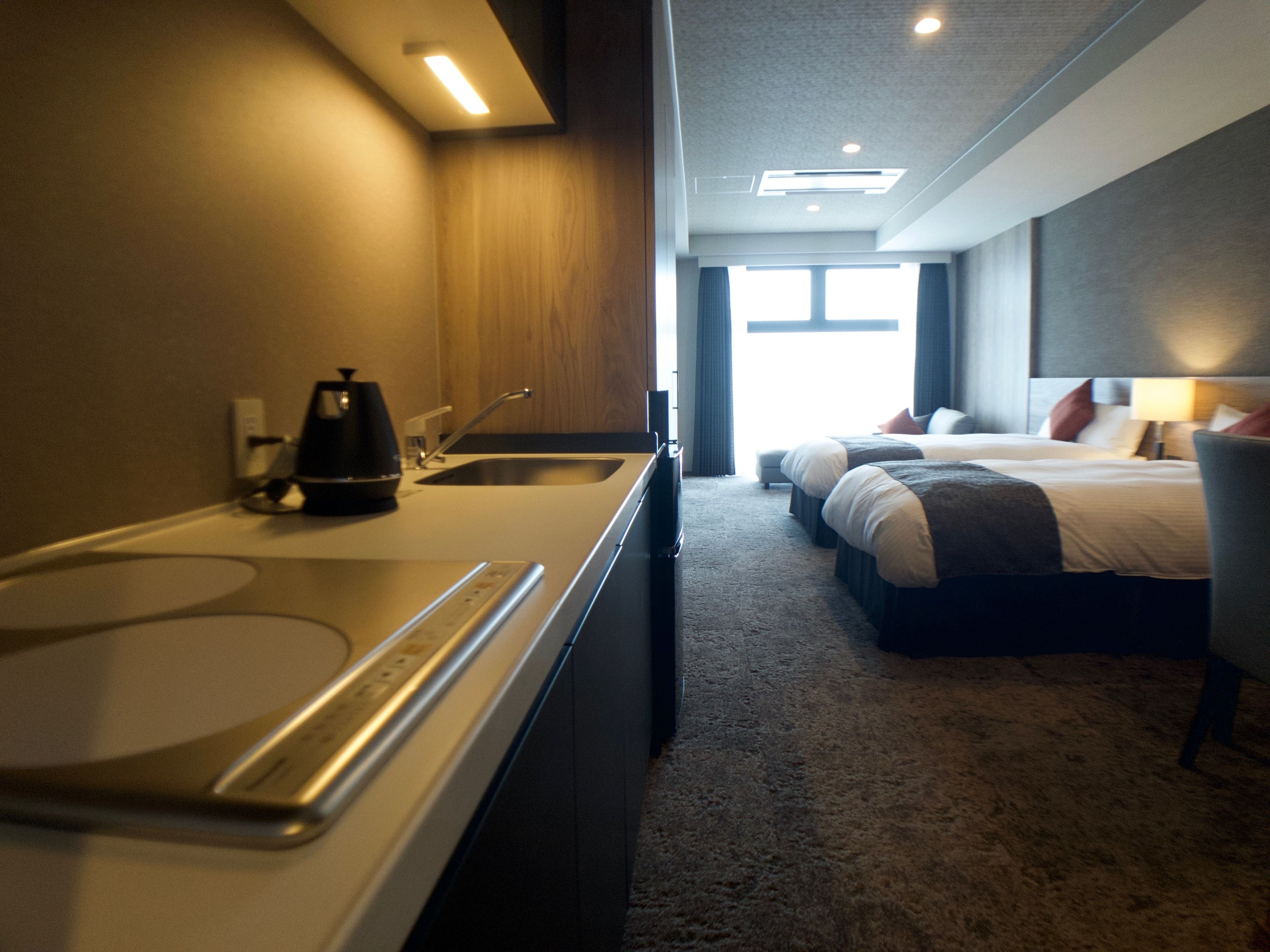 Quarto de hotel moderno com cozinha compacta, uma cama grande e vista para o exterior.