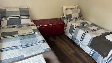 Quarto com duas camas, um banquinho vermelho e uma toalha branca no chão.