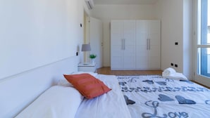 Quarto com cama, mesa de cabeceira, luminária, guarda-roupa e janela.