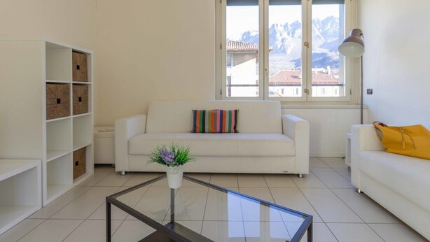 Sala de estar moderna com um sofá branco, uma mesa de centro de vidro e vista para montanhas por uma janela grande.