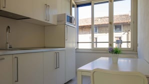 Cozinha com armários brancos, micro-ondas e janela com vista para edifícios.