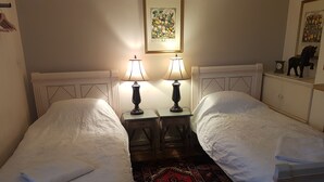 Quarto com duas camas de solteiro, uma mesa pequena com duas luminárias, um tapete estampado e um relógio na parede.