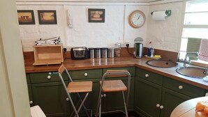 Cozinha compacta com armários verdes, bancada de madeira, pia e um relógio.