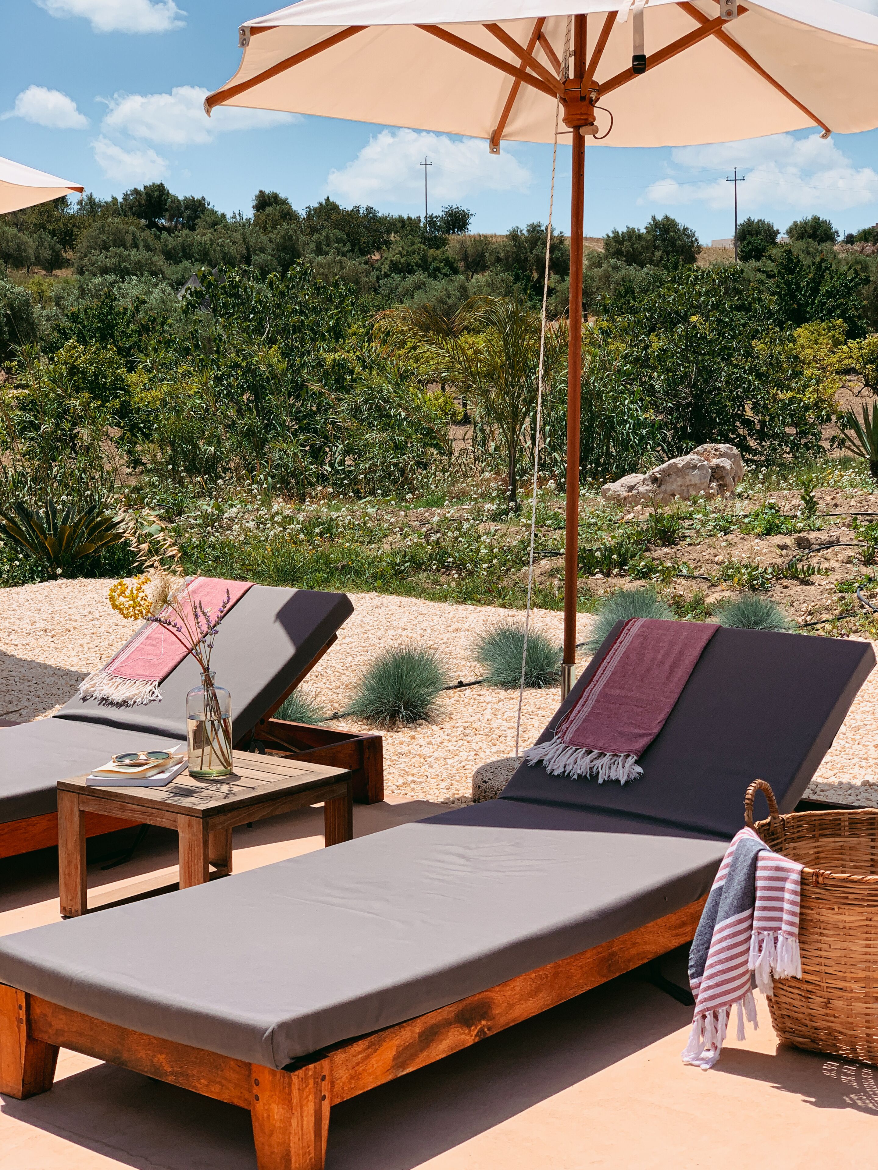 Uma área externa ensolarada com assentos de estar, cadeiras de descanso, uma mesa e um grande guarda-sol.