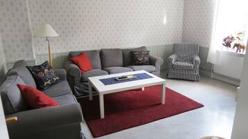 Sala de estar com sofá cinzento, tapete vermelho, mesa de centro branca e parede estampada.