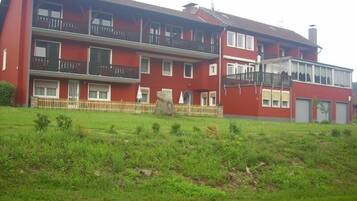Um edifício residencial vermelho de vários andares, com varandas, cerca de madeira e gramado frontal.
