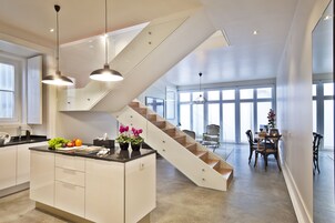 Uma cozinha moderna com ilha central, escada e área de refeições com iluminação natural.