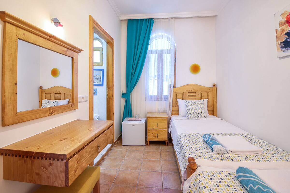 Quarto com escrivaninha de madeira, cama com roupa de cama estampada, mesa de cabeceira e pequena mesinha de apoio.