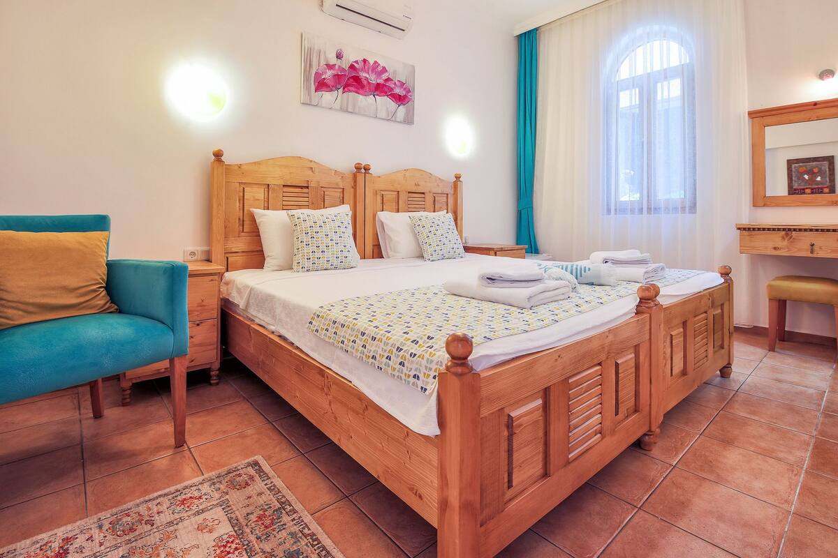 Quarto bem organizado com cama de madeira, poltrona azul e escrivaninha com espelho.