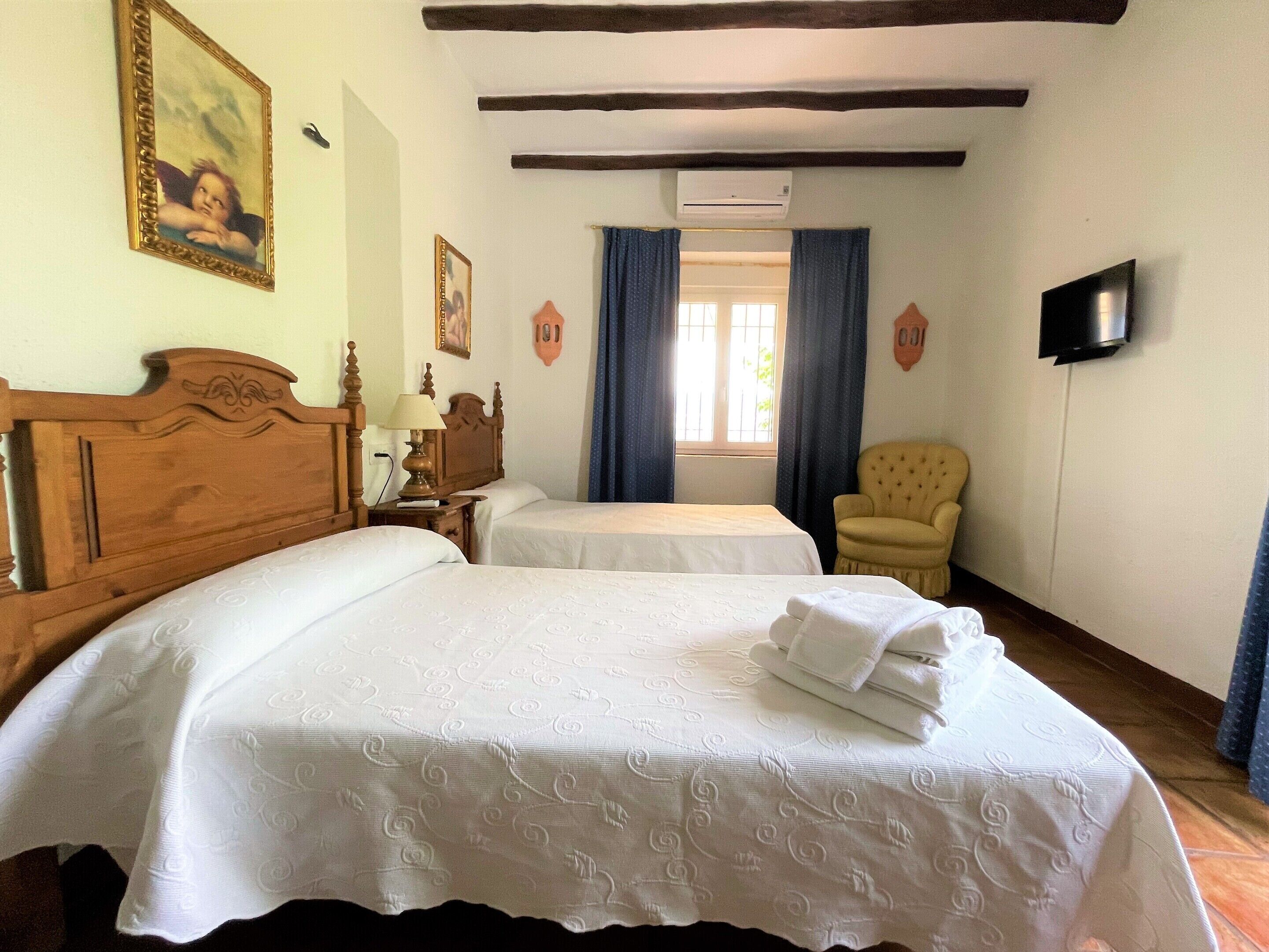 Quarto de hotel com duas camas, uma cabeceira de madeira, uma cadeira, uma televisão e uma janela com cortinas.